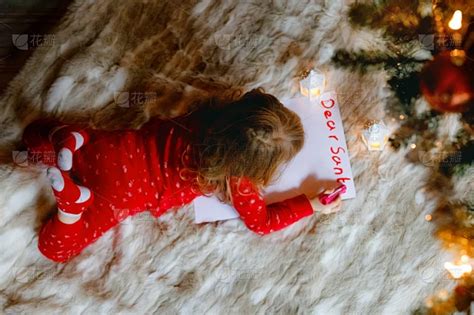 可爱的小女孩躺在圣诞树下的床上，在家给圣诞老人写愿望单。传统的基督教节日。快乐的孩子等待圣诞礼物。素材 花瓣网