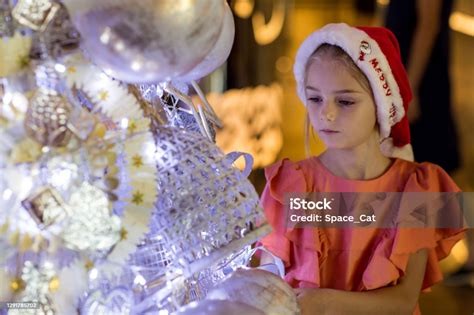 산타 모자를 쓰고 아늑한 흰색 크리스마스 트리를 장식하는 작은 귀여운 소녀 메리 크리스마스와 해피 홀리데이 12월에 대한 스톡 사진 및 기타 이미지 Istock