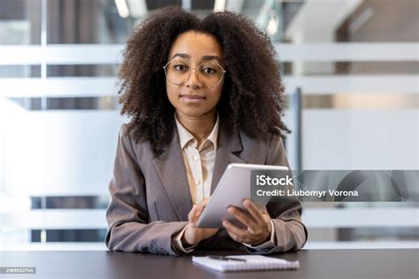 안경과 양복을 입고 사무실 책상에 앉아 태블릿을 들고 카메라를 바라보며 웃고 있는 젊은 아프리카계 미국인 여성의 클로즈업 초상화 가상현실에 대한 스톡 사진 및 기타 이미지