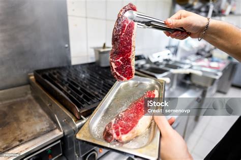 집게를 사용하여 마블링이 있는 생 스테이크를 전문 주방의 뜨거운 그릴에 올려놓는 셰프의 손 스테이크는 그릴에 닿으면서 지글지글