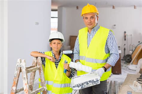 노란 조끼와 보호 헬멧을 입은 아버지와 아들의 초상화 페인트 롤러로 방의 벽을 칠하는 사람 2명에 대한 스톡 사진 및 기타 이미지 Istock
