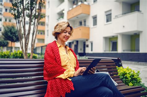 공원에서 벤치에 앉아 태블릿을 사용하여 금발 짧은 머리와 매력적인 미소 백인 유행 고위 여성의 측면보기 40 49세에 대한 스톡 사진 및 기타 이미지 Istock