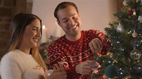 دانلود فوتیج ویدیویی زوج جوانی که درخت کریسمس را با هم تزئین می کنند استوک فوتیج