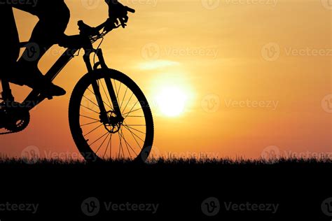 Silhouette Of Cyclist Riding Bike At Sunset With Vibrant Orange Sky And