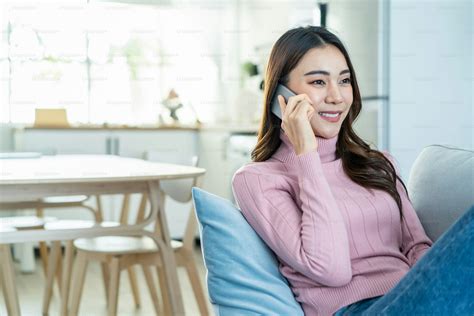 아시아의 아름다운 여자는 소파에 앉아 집에서 휴대폰으로 이야기한다 행복하고 매력적인 어린 소녀는 집에서 여가 시간을 보내고 휴식을 취하고 거실에서 스마트 폰으로 의사