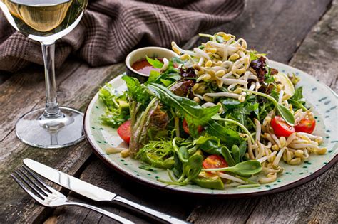 Arugula 양상추 발아 곡물 토마토 아보카도 녹두 샐러드 및 오이를 칼 붙이와 와인 한 잔과 함께 테이블 위의 접시에 샐러드 0명에 대한 스톡 사진 및 기타 이미지