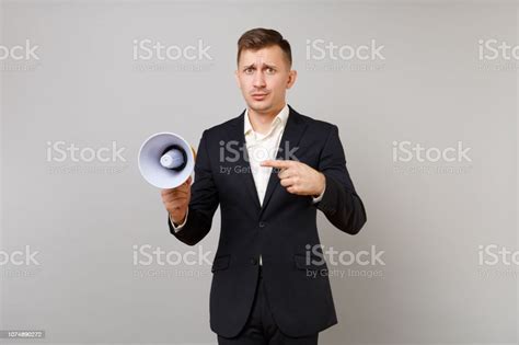 클래식 블랙에 당황한 젊은 사업가 셔츠 스튜디오에 회색 벽 배경에 고립 된 확성기에 포인팅 검지 손가락에 맞게 성과 경력 부