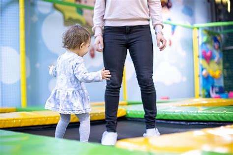 어머니와 함께 트램폴린에 점프하고 웃고 있는 드레스를 입은 귀여운 유아 소녀 어린이 놀이 센터의 어린이 놀이터에서 백 뷰 흐린 배경 아기에 대한 스톡 사진 및 기타 이미지