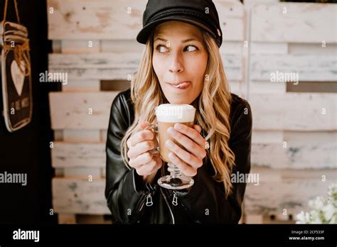 Long Haired Trendy Woman Holding Glass Of Delicious Foamy Coffee Licking Lips Anticipating