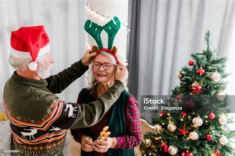 산타 모자와 의상 순록 뿔을 입고 집에서 함께 크리스마스를 축하하는 재미를 느끼는 노인 부부 12월에 대한 스톡 사진 및 기타 이미지 Istock