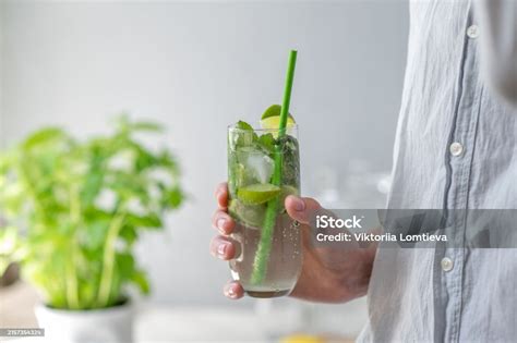 중립 회색 벽 배경 여름 상쾌한 음료 부드러운 자연 햇빛 라이프 스타일에 얼음 민트 라임 및 녹색 마시는 빨대와 함께 모히토 칵테일 음료와 함께 유리를 들고 있는 사람 손