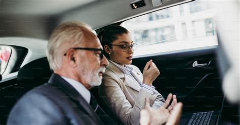 잘 생긴 고위 사업가와 그의 젊은 여성 동료 또는 동료가 고급 자동차의 뒷좌석에 앉아 있습니다 그들은 이야기하고 웃고 노트북과 스마트 폰을 사용합니다 기업 비즈니스