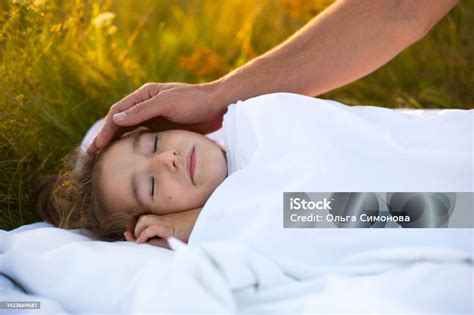 소녀는 풀밭의 하얀 침대에서 자고 신선한 공기를 마신다 아빠의 손이 부드럽게 머리를 두드린다 보살핌 보호 국제 어린이날 모기에 물린 2명에 대한 스톡 사진 및 기타 이미지