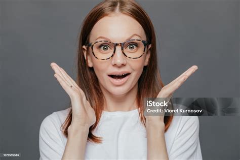 와우 그건 좋은 놀란된 기쁘게 아름 다운 여자 즐거운 모습 얼굴 가까이 손바닥을 확산 궁금해 캐주얼 티셔츠 회색 스튜디오 배경 위에 절연 입고에서 입을 감정에 대한 스톡