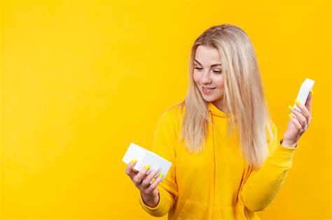 노란 스포츠 복을 입은 젊은 백인 금발 여성의 초상화가 노란 배경에 고립된 흰색 선물 상자를 열고 미소를 지으며 상자를 바라보고 있습니다 복사 공간 감정에 대한 스톡 사진