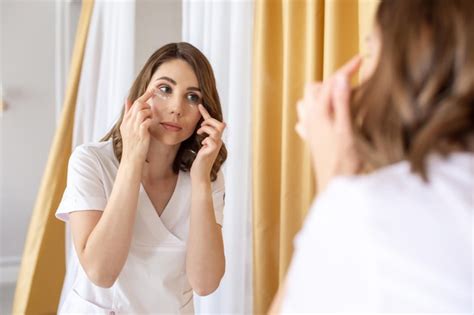 Linda Chica Se Mira En El Espejo Y Aplica Crema Para Los Ojos Foto