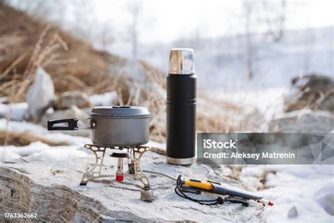 숲 속에서 생존을 위한 캠핑 장비 세트 등산 캠프 요리 요리 차가 담긴 검은 보온병 가스 버너 위에 서 있는 냄비 칼 눈 냉동상태의 물에 대한 스톡 사진 및 기타 이미지