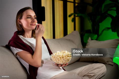 Женщина Ест Попкорн И Смотрит Телевизор Сидя Дома На Диване — стоковые фотографии и другие