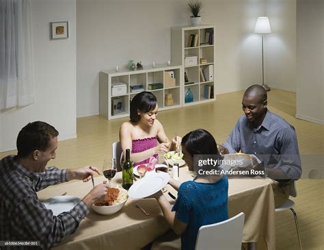 Four Young People Sitting Around Dinner Table And Eating Elevated View