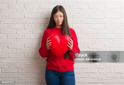 스마트 얼굴 심각한 생각에 자신감 표현 붉은 마음을 잡고 하는 벽돌 벽을 통해 사랑에 젊은 중국 여자 감정에 대한 스톡 사진 및 기타 이미지 Istock