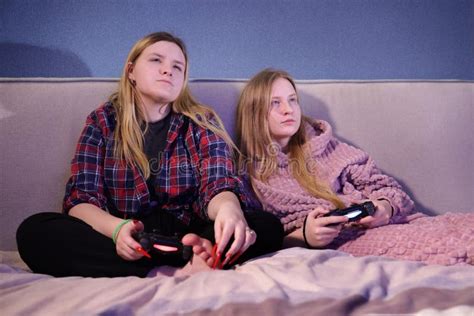 Two Teen Girls Playing Video Games On A Bed Both Intensely Focused On