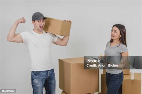 이두근을 구부려 자신의 힘을 보여주는 상자 상자를 들고 젊은 잘 생긴 배달 남자 여자는 그를 흥분보고있다 2명에 대한 스톡 사진 및 기타 이미지 Istock