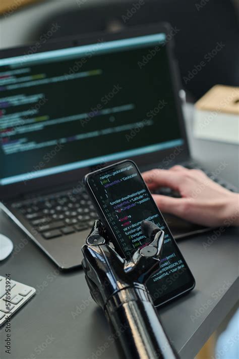 Vertical Image Of Programmer With Prosthetic Arm Connecting Smartphone With Laptop And Typing