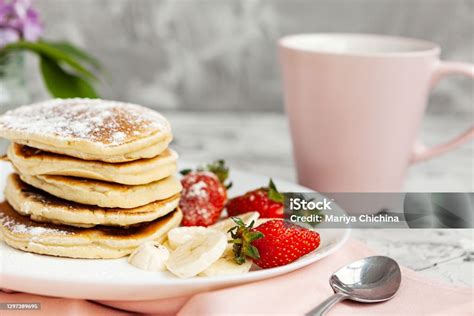 밝은 배경에 흰색 접시에 분홍색 차 찻잔과 신선한 딸기가있는 팬케이크 더미 아침 식사 옆에는 유리 꽃병에 담긴 작은 라일락 꽃다발이 있습니다 건강한 생활방식에 대한 스톡