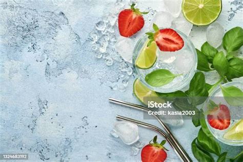 레모네이드 주입 된 해독 물 또는 칵테일을 만들기위한 펀치와 신선한 재료 두 잔 회색 돌 또는 콘크리트 배경에 딸기 라임 민트 바질 얼음 조각과 셰이커 맨 위 보기입니다 0