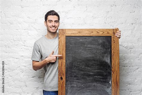 Attractive Babe Man Pointing At Blackboard Handsome Male Standing Against White Brick Wall