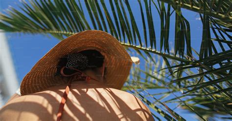 여름 휴가를 즐기는 수영장에서 휴식을 취하는 모자를 쓴 아름다운 여성의 뒷면에 야자수 잎의 그림자가 있습니다 피부 관리 및