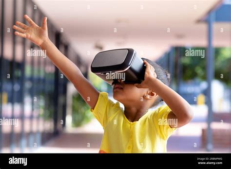 Biracial Schoolgirl Using Vr Headset Reaching Out Hand In Sunny School Corridor With Copy Space