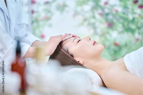 Foto De 아시아 한국의 젊은 한국여성 모델은 거즈를 이용해 스파 또는 피부관리전문점 또는 피부과 병원의 침대에 누워서 전문관리사에게 머리와 얼굴을 관리를 받음 Do