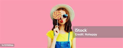 롤리팝이 입술을 불고 핑크색 배경에 밀짚 모자를 쓰고 달콤한 공기 키스를 보내는 세련된 젊은 여성의 여름 초상화 20 29세에 대한 스톡 사진 및 기타 이미지 Istock