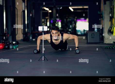 Athletic Arab Man Making Dumbbell Push Ups While Recording Content On Smartphone Camera Stock
