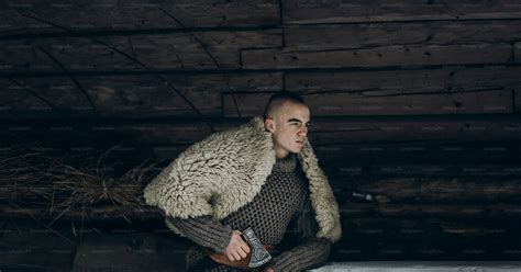 전쟁 전에 도끼를 든 강하고 화난 바이킹 전사 고대 스칸디나비아 전사 코스프레 토르 의상 북부 벌목꾼 의상 목조 건물 근처에 있는 남자의 자신감 넘치는 표정 사진