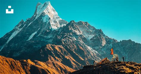 낮에는 눈 덮인 산 근처의 갈색 바위에 서 있는 주황색 재킷을 입은 사람 사진 Unsplash의 무료 사람의 이미지