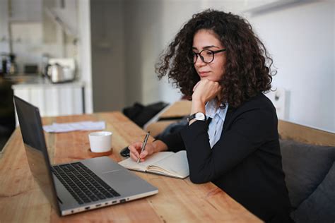 사무실에서 노트북 컴퓨터를 보고 메모를 하는 사업가 노트북에서 작업하는 동안 테이블에 앉아 메모를 작성하는 여성 기업가 검사 보기에 대한 스톡 사진 및 기타 이미지 Istock