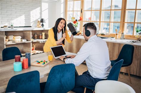 남편이 노트북에서 작업하려고하는 동안 집에서 노래하고 춤을 추고 무선 블루투스 스피커를 들고있는 여성 가정 생활에 대한 스톡