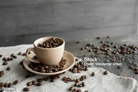 신선한 아라비카 또는 로부스타 커피 콩이 린넨 섬유와 목재 테이블에 흩어져 있는 커피 원두로 채워진 커피 컵 콩 콩과에 대한 스톡 사진 및 기타 이미지 Istock
