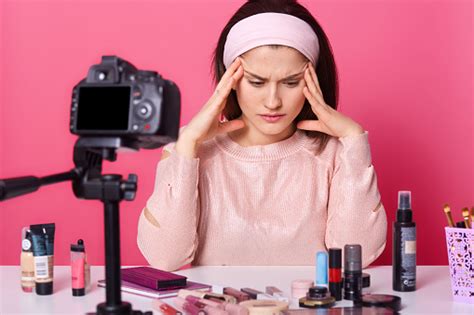 분홍색 스웨터와 머리 띠를 착용 하 고 테이블 표면을 보고 손가락으로 사원을 만지고 혼란 스 러 워 지 고 스튜디오에서 분홍색