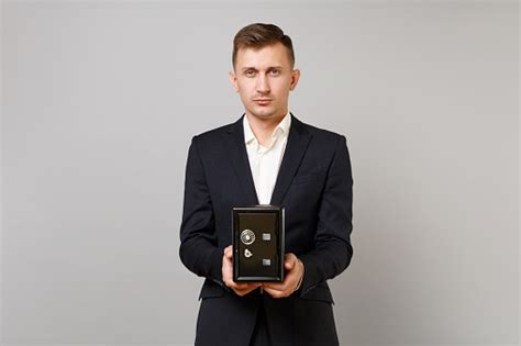 고전적인 검은 양복에 젊은 사업가 금속 은행 돈 축적 스튜디오에서 회색 벽 배경에 고립에 대 한 안전 하 게 잡고 축구 성과 경력 부 비즈니스 개념입니다 복사 공간을 비웃는