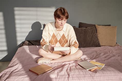 캐주얼 스웨터에 심각한 빨간 머리 학생 소녀 앉아 교차 다리 와 함께 침대 사이 책 사이 스케치 패드에 메모를 검사 16 17 살에 대한 스톡 사진 및 기타 이미지 Istock