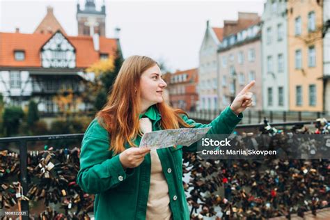 배낭을 멘 젊고 예쁜 30대 여성이 종이 지도를 들고 복사 공간의 물체를 가리키고 있는 모습 밀러스 길드 하우스와 그단스크의 라두니아 운하를 배경으로 한 뒷모습 Tri