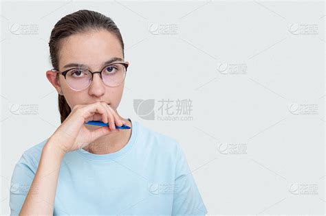 沉思的迷人的女学生在她的嘴里拿着一支笔，看着你在白色的背景与复制空间