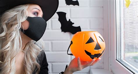 검은 마녀 의상을 입은 슬픈 금발과 얼굴 마스크가 창문 밖을 바라 봅니다 코비드로부터 할로윈 보호 준비 10월에 대한 스톡 사진