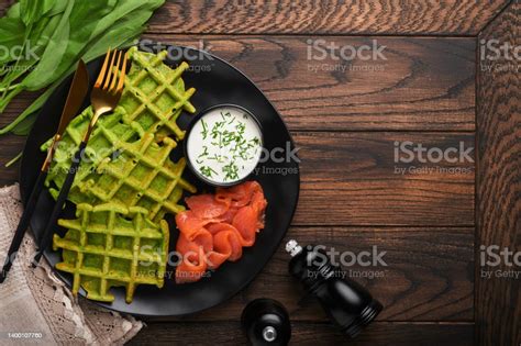 녹색 벨기에 와플 시금치 또는 야생 마늘 또는 페스토 와플과 붉은 연어와 크림 소스를 어두운 소박한 나무 배경 위에 검은 접시에 올려 놓습니다 맛있는 아침 식사 스낵 브런치