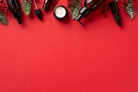 유기농 화장품 개념입니다 호박색 유리 펌프 병 크림 항아리 점 적기 병 겨우살이 열매와 소나무 가지의 상위 뷰 사진은 빈 공간이 있는 격리된 빨간색 배경에 있습니다