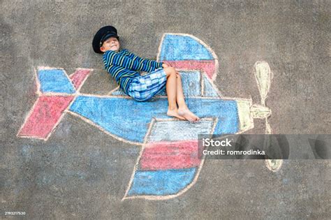 아스팔트에 다채로운 분필로 비행기 그림 그리기를 가지고 놀고 있는 어린 아이 소년 분필로 그림을 그리거나 휴가를 가거나 조종사