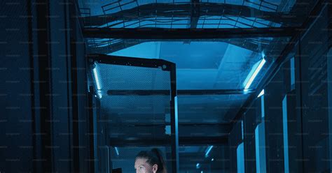 Female It Manager With Cellphone Checking Hardware On Server Racks In